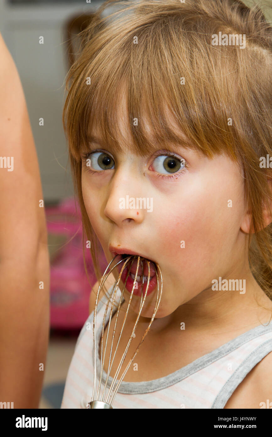 Little girl licking chocolate off the mixer beater after mixing dough ...