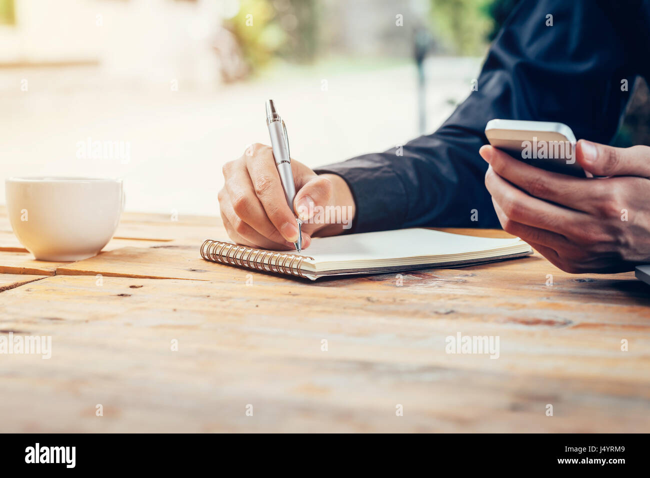 Asia man hand writing notebook paper and using phone on wood table in ...
