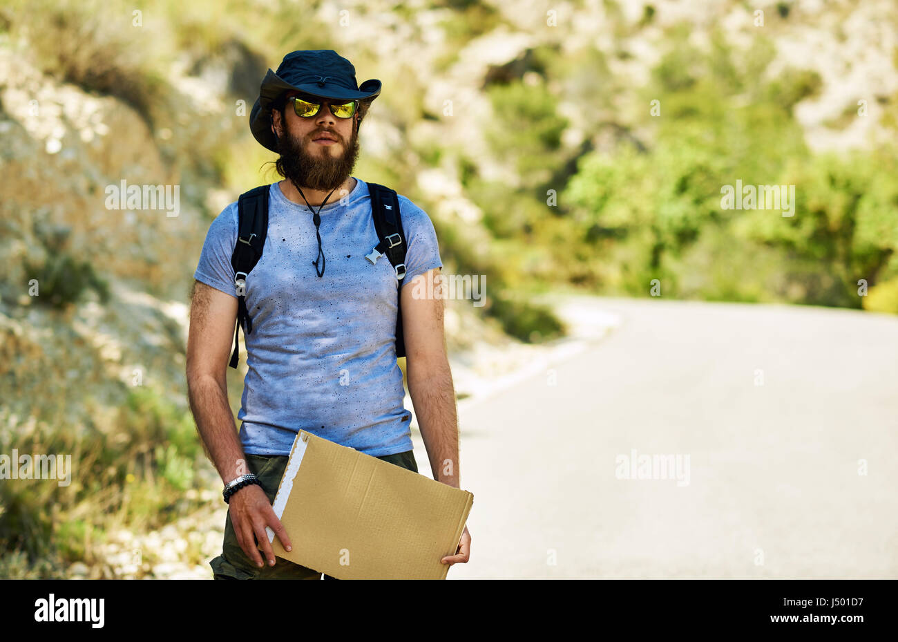 Hitch-hiking traveler with a blank cardboard sign on a mountain road ...