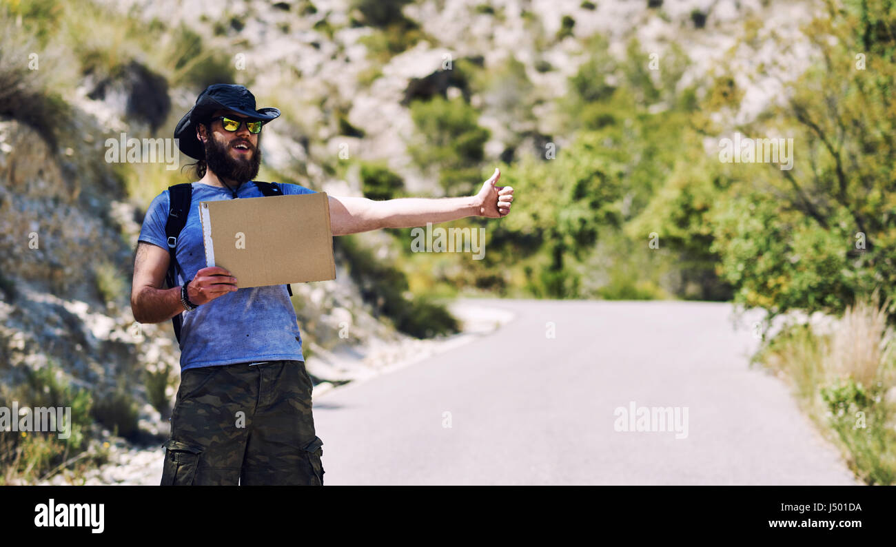 Hitch-hiking traveler with a blank cardboard sign on a mountain road ...