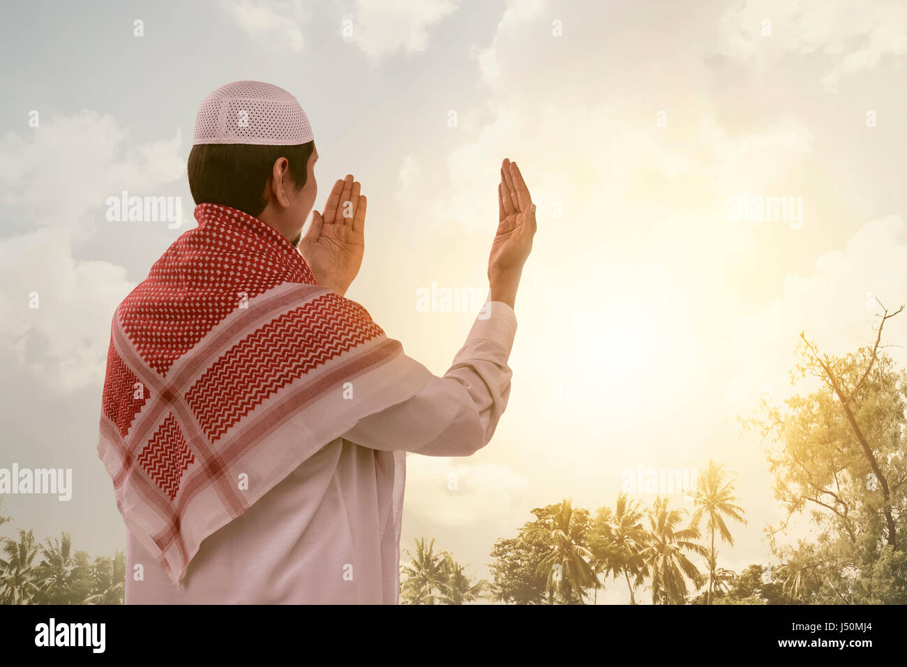 Back view of asian muslim man in white cap praying with sunlight ...