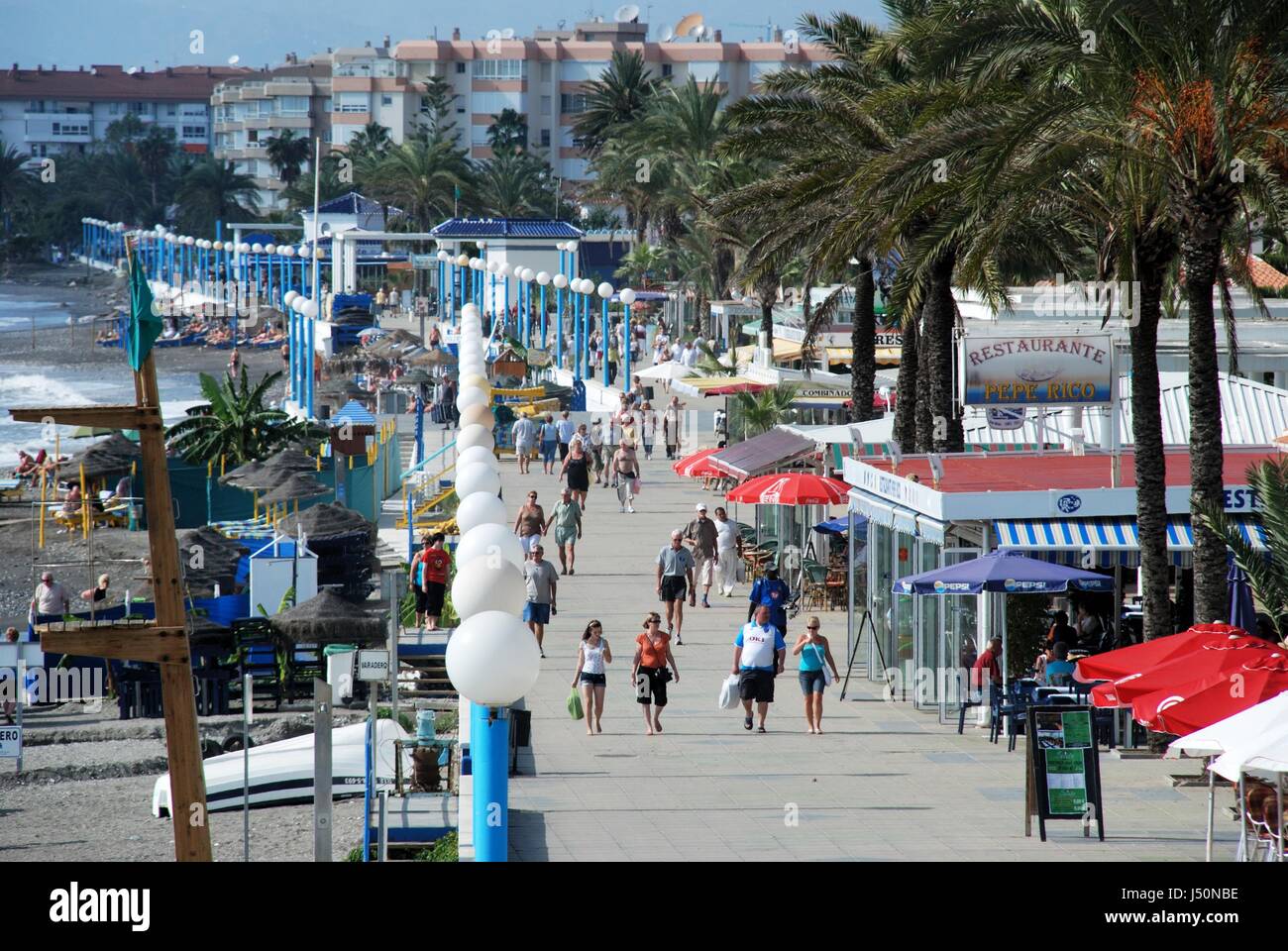 Tourists walking along the promenade with pavement cafes to the right ...