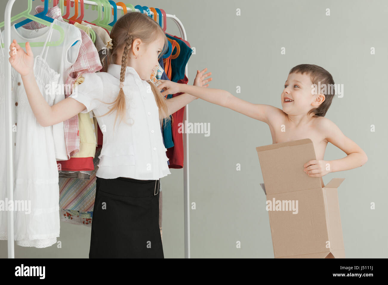 Two little children standing near a hanger with clothes at home at the ...