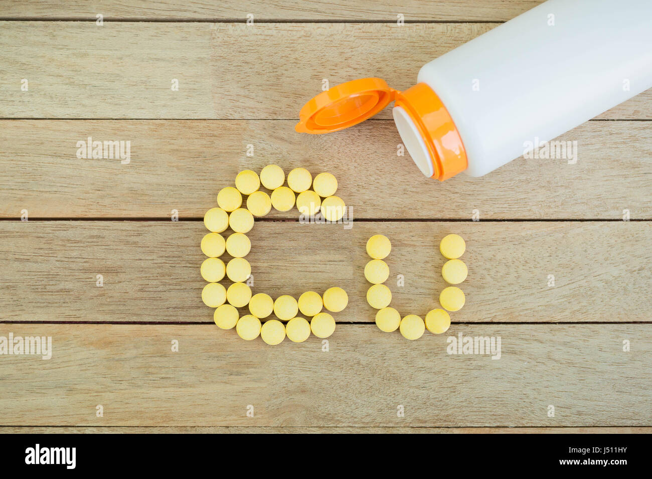 Yellow pills forming shape to Cu alphabet on wood background Stock ...