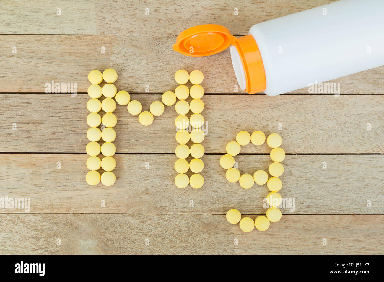 Yellow pills forming shape to Mg alphabet on wood background Stock ...