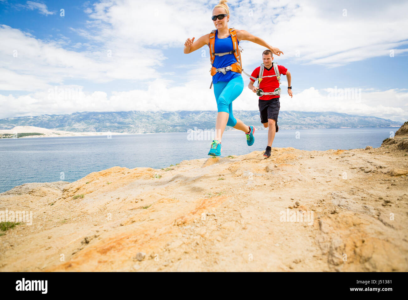 Couple runners running with backpacks on rocky trail at seaside and ...