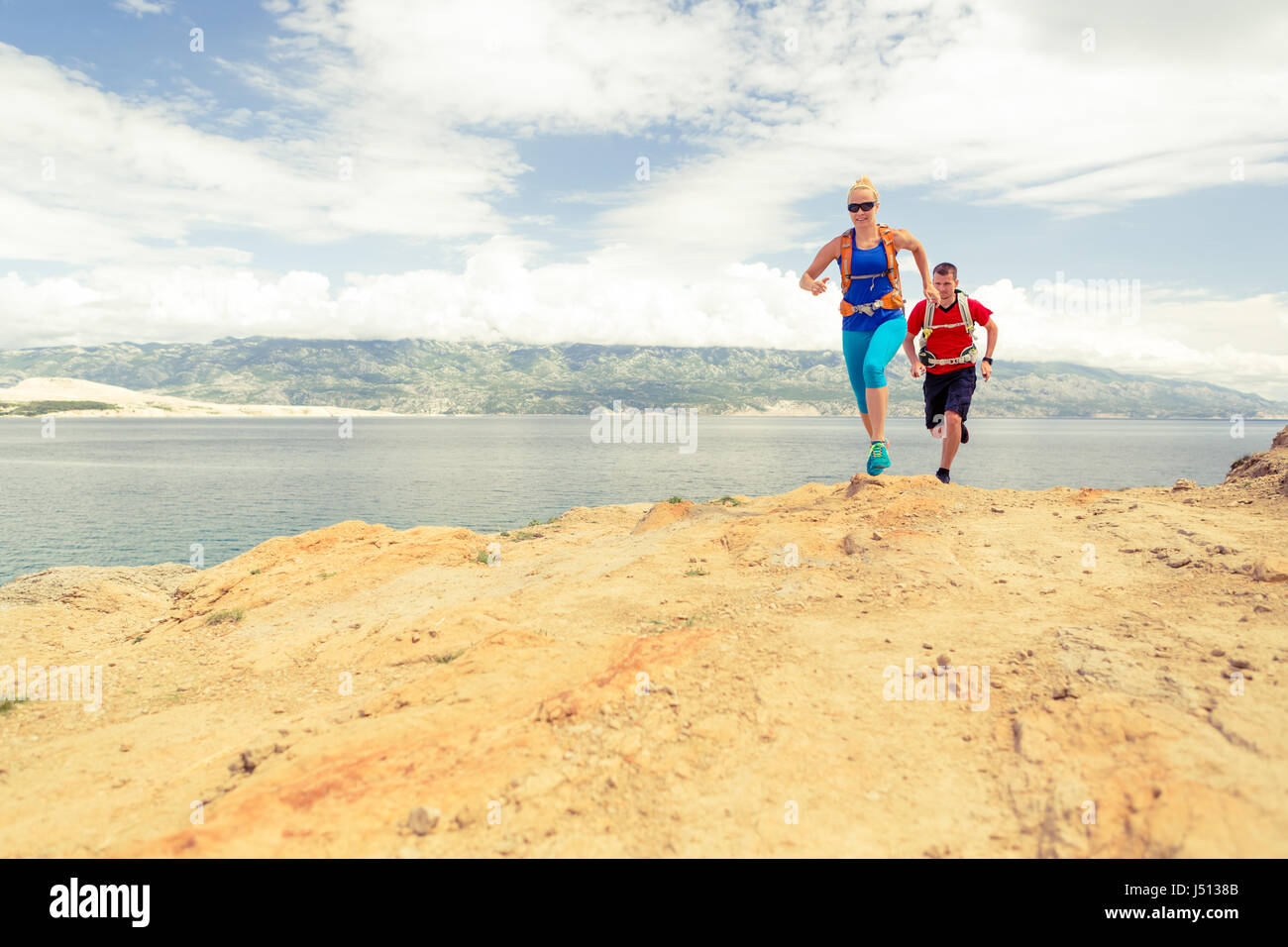 Couple runners running with backpacks on rocky trail at seaside and ...
