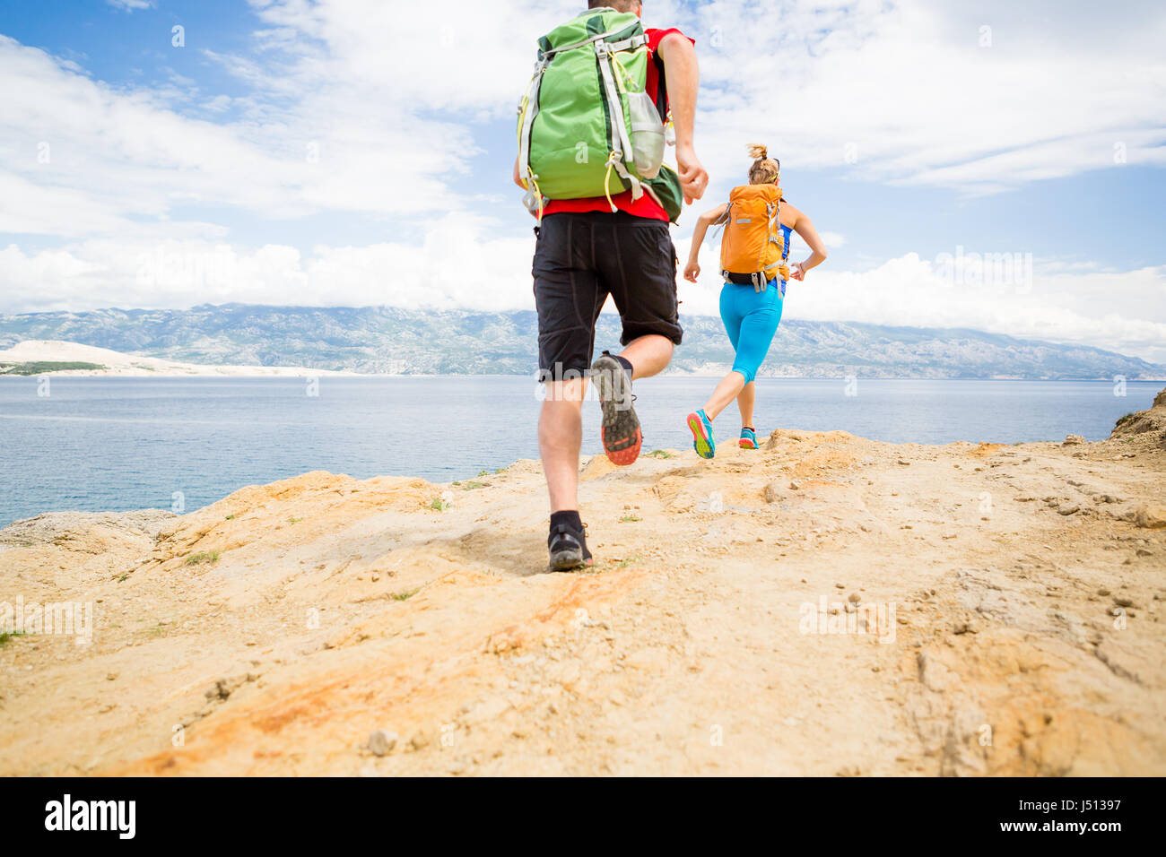 Couple runners running with backpacks on rocky trail at seaside and ...