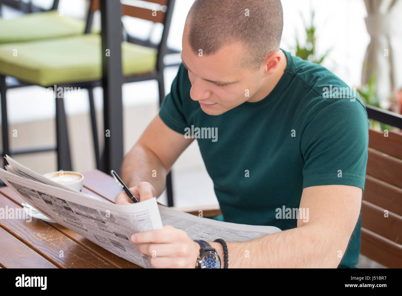 Young man sits at a table, carefully reading the newspaper ads and ...