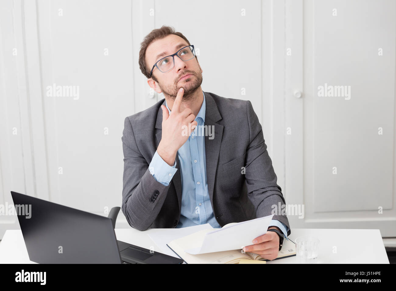 Businessman at the desk, looking up and thinking Stock Photo - Alamy