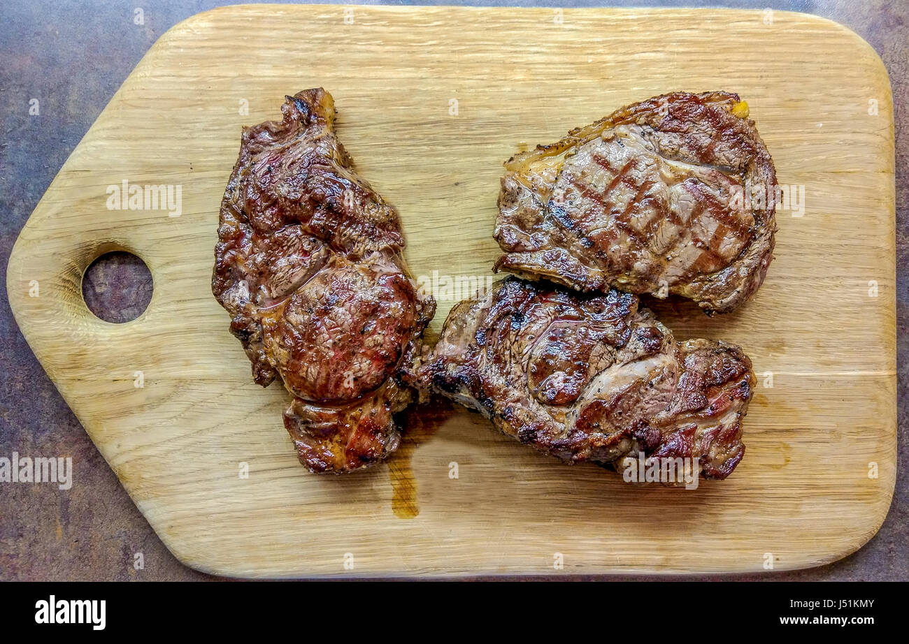 Three rib eye steaks cooked on a grill . They are on the wooden desk ...