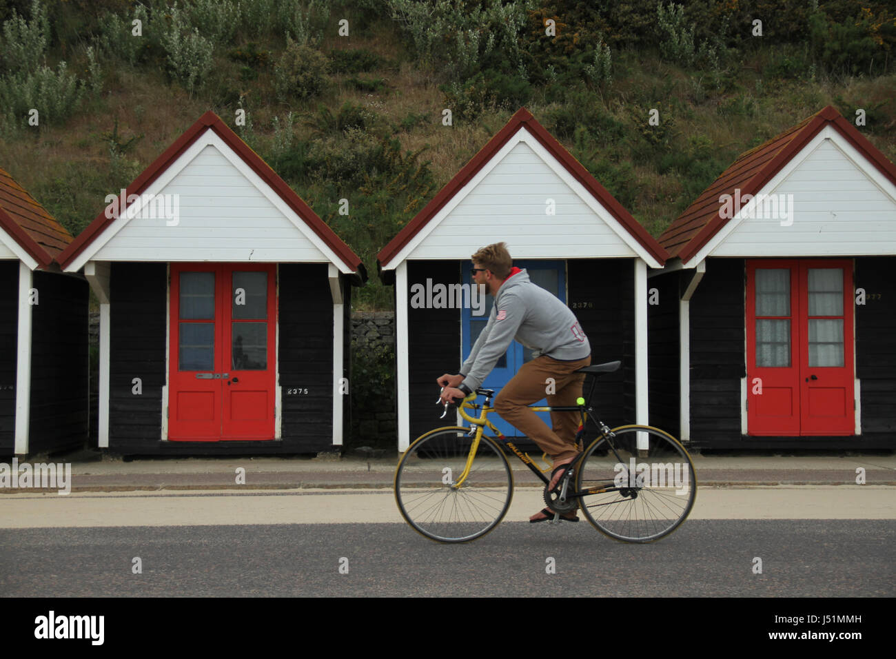 Bournemouth, UK - 11 May: A cyclist rides past an array of beach huts ...