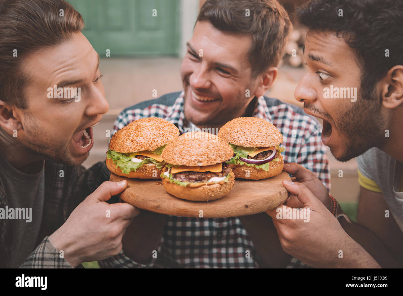 Side view of excited young men biting fresh tasty hamburgers Stock ...