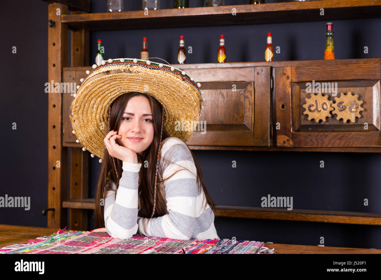 Beautiful young woman in a sombrero leaned on bar counter in Mexican ...