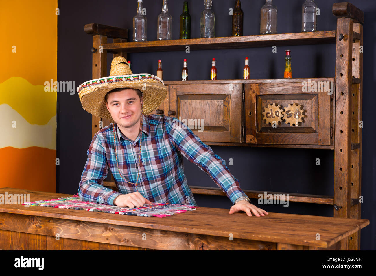 Smiling young man as bartender in a sombrero leaned on bar counter in ...