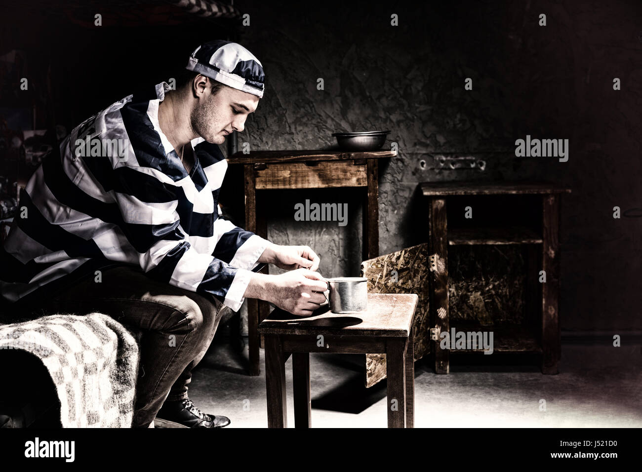 Male prisoner wearing prison uniform sitting on a bed and eating from ...