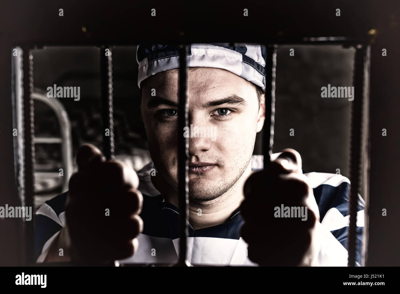 View through iron door with prison bars on young prisoner holding bars ...