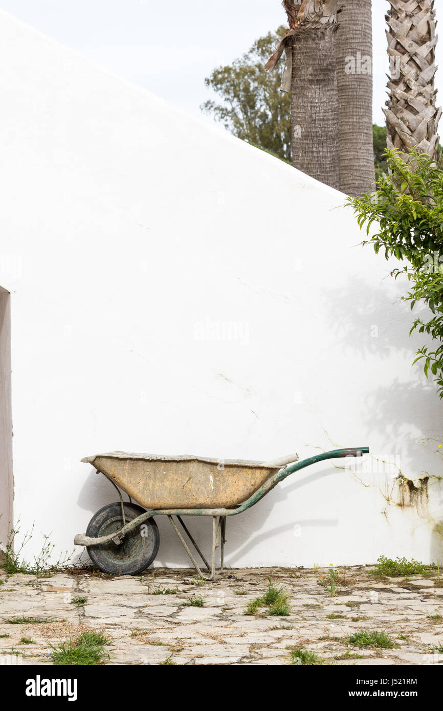old muddy garden wheelbarrow with white wall Stock Photo - Alamy