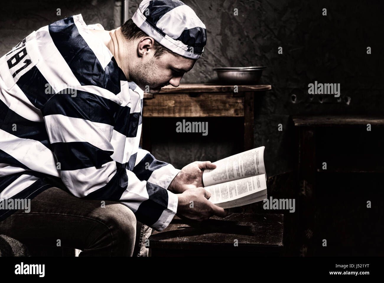 Male prisoner wearing prison uniform reading a book or a bible while ...
