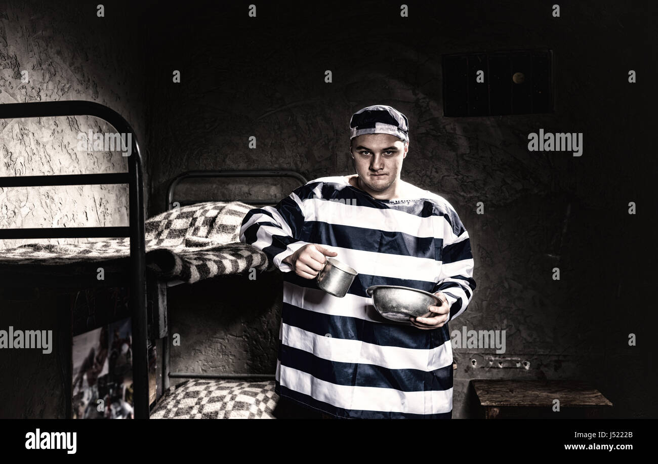 Angry prisoner wearing prison uniform holding aluminum dishes standing ...