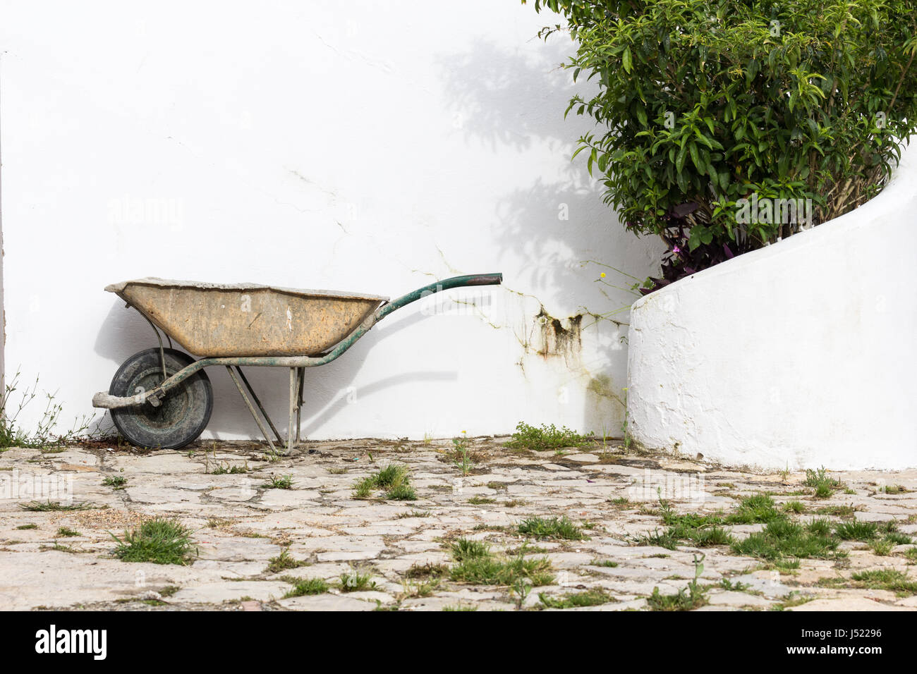 closeup old muddy garden wheelbarrow with white wall Stock Photo - Alamy