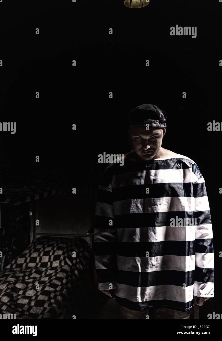 Aggressive male prisoner wearing prison uniform standing near his bed ...