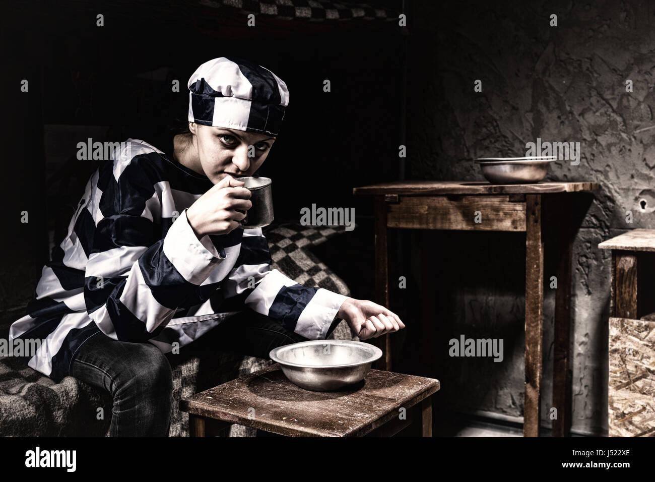 Angry female prisoner wearing prison uniform sitting on a bed and ...