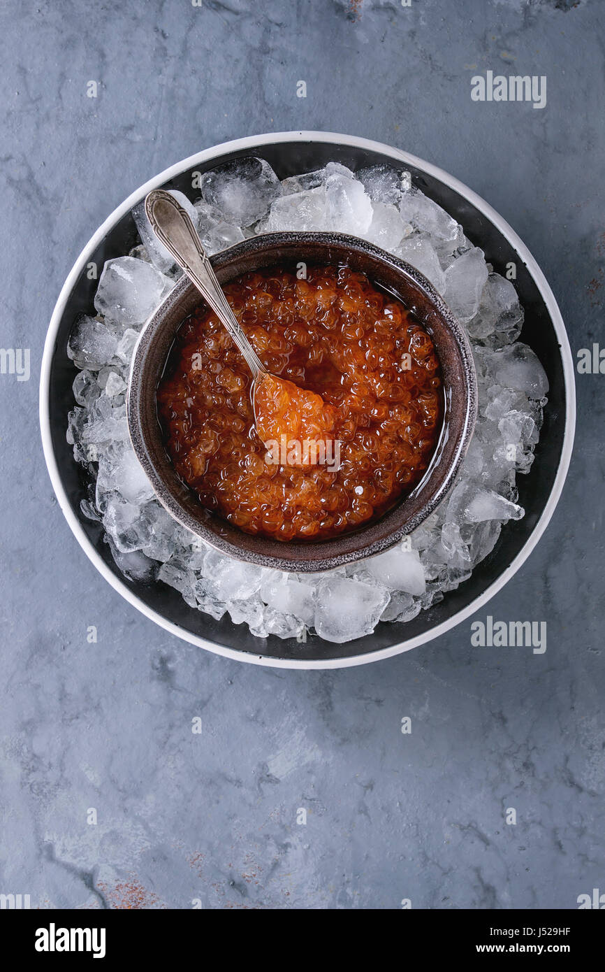Bowl of red caviar on ice with spoon served over gray blue texture ...
