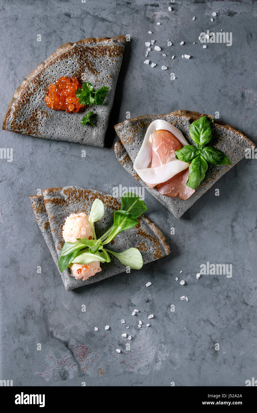 Black pancakes crepes with variety of salt filling red caviar, ham ...
