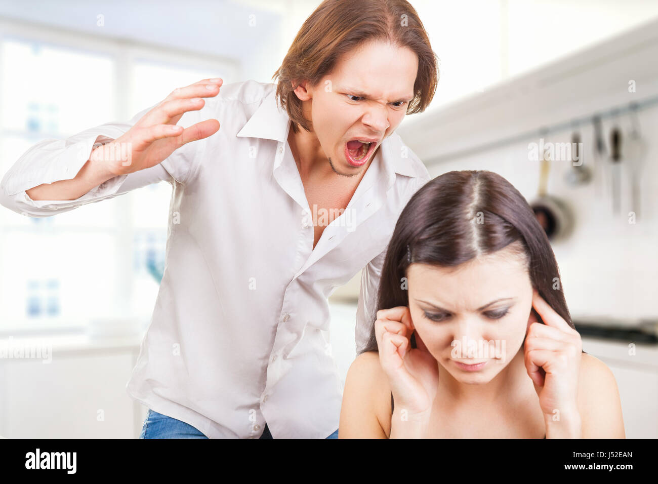 Enraged man shouts at the young woman in the kitchen. Woman covering ...