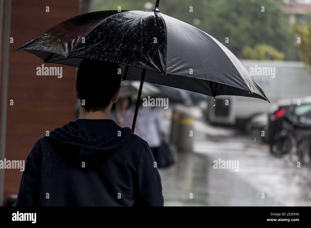 Man with umbrella covering from the rain. Rear view. From behind. Real ...