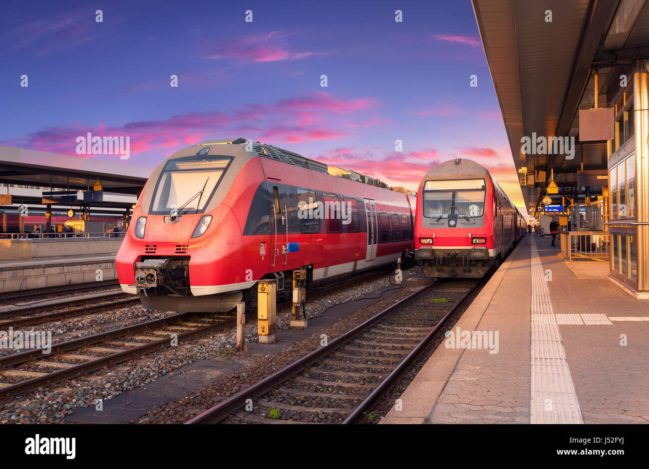 High speed red commuter trains on railway station and colorful sky at ...