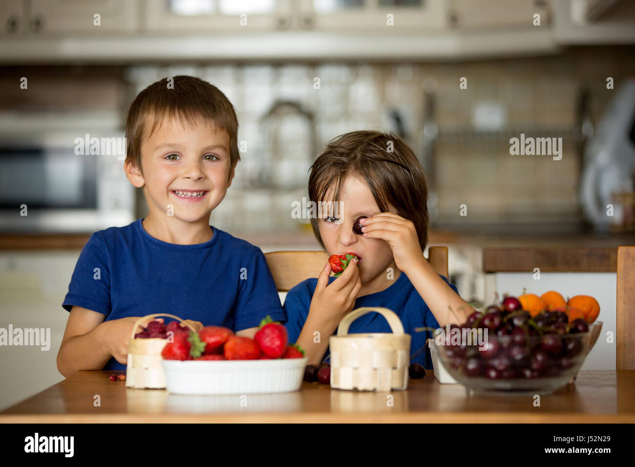 Two sweet children, boy brothers, eating fresh fruits at home ...