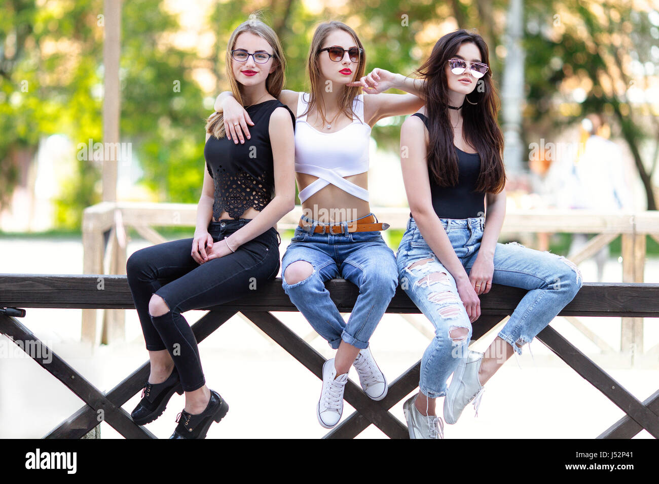 Three girls with shopping bags on park blur background Stock Photo - Alamy