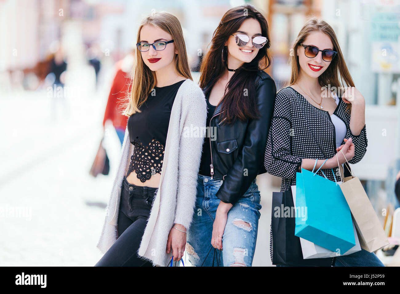Three girls with shopping bags on park blur background Stock Photo - Alamy