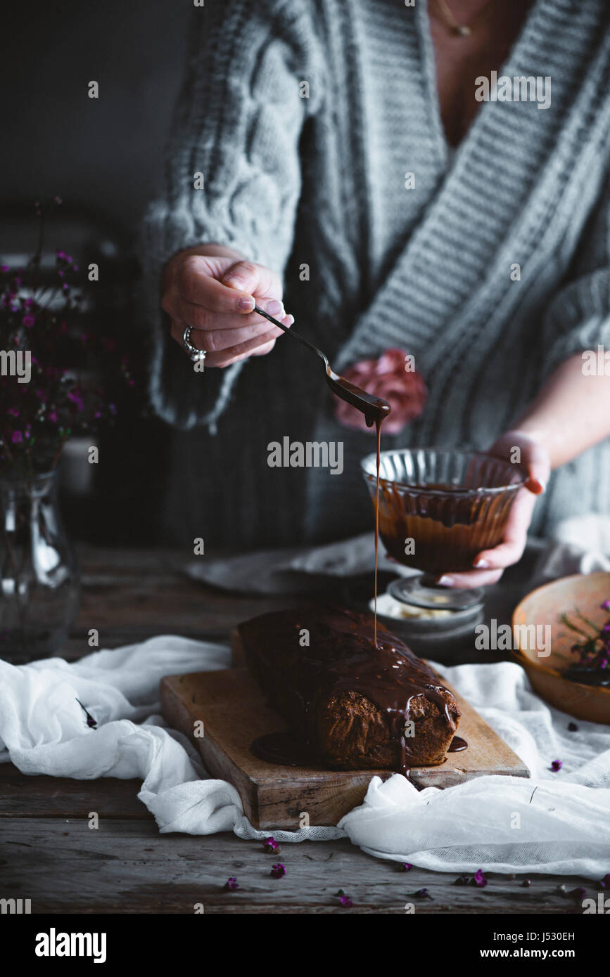 A woman pouring chocolate icing over a cake in a country kitchen Stock ...