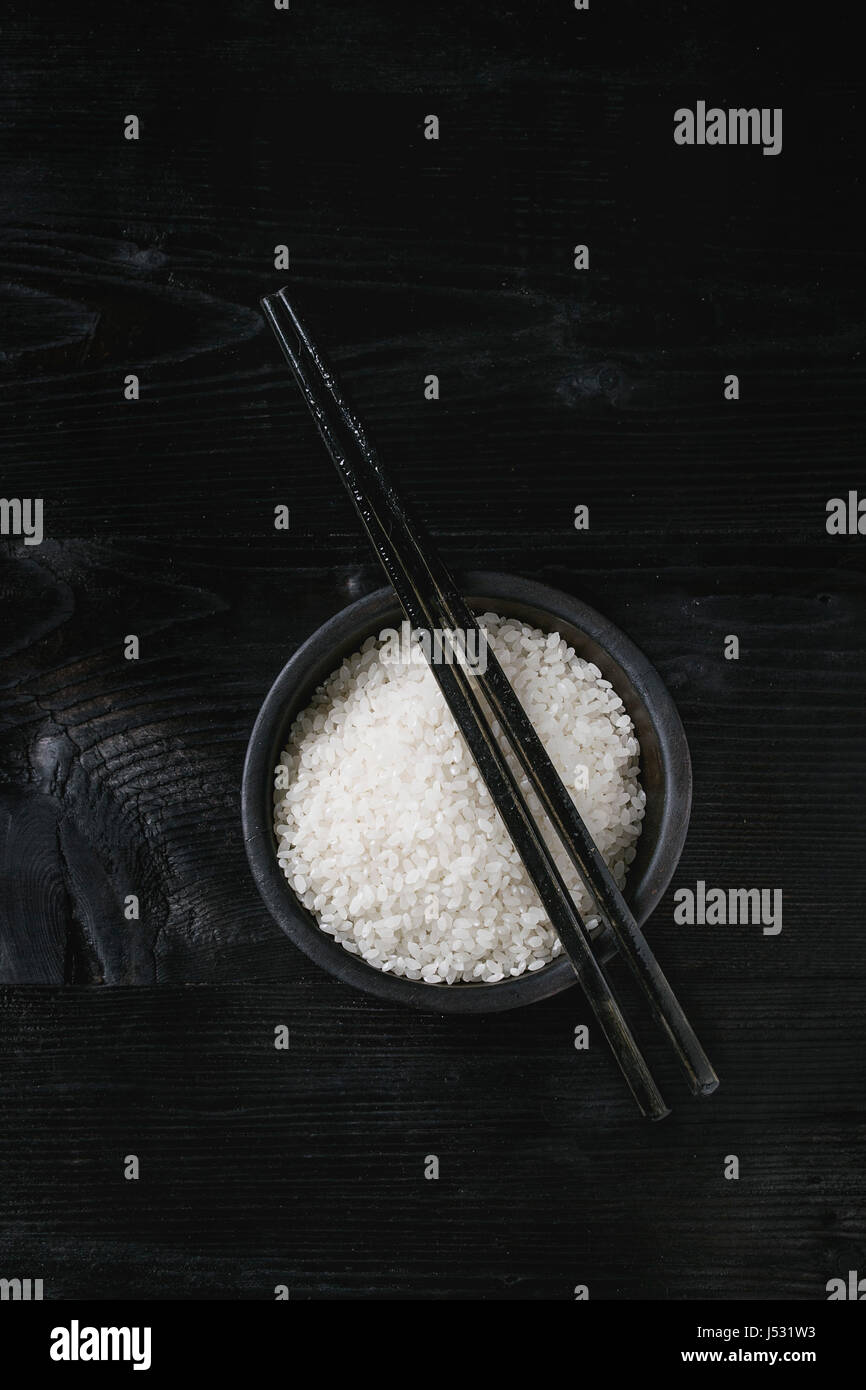 White sushi raw uncooked rice in black bowl with chopsticks over burnt ...