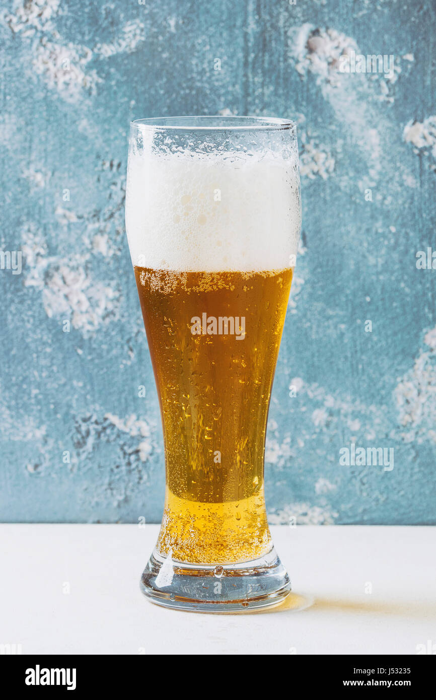 Glass of lager beer with foam on white table with blue texture concrete ...
