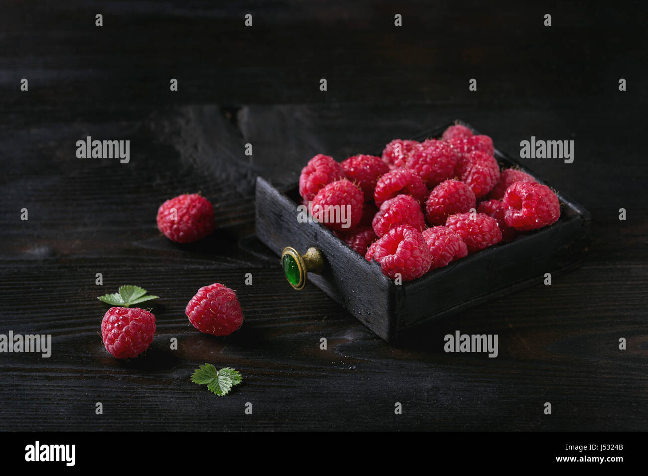 Fresh organic wet ripe raspberries in black wood box over wooden burnt ...