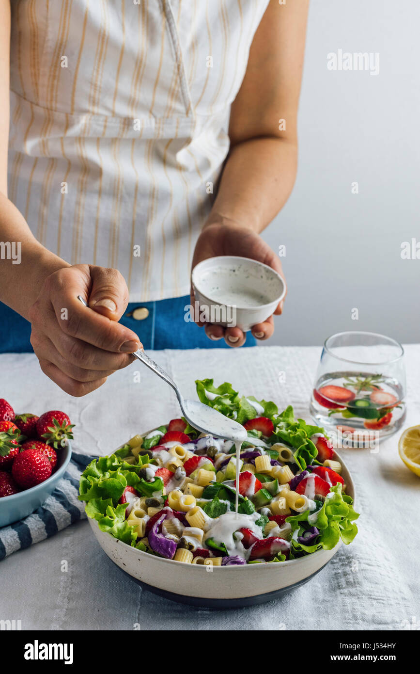 A woman drizzling yogurt dressing over a fresh strawberry pasta salad ...