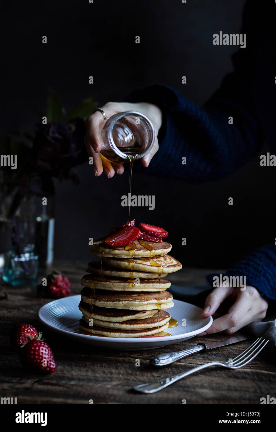Woman pouring maple syrup on the pancakes with strawberries Stock Photo ...