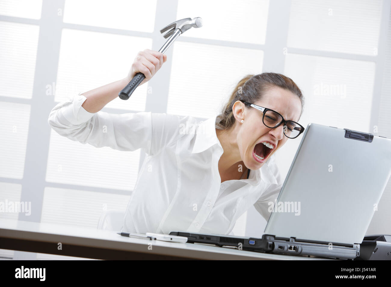 Freaked out businesswoman with a hammer ready to smash her laptop ...