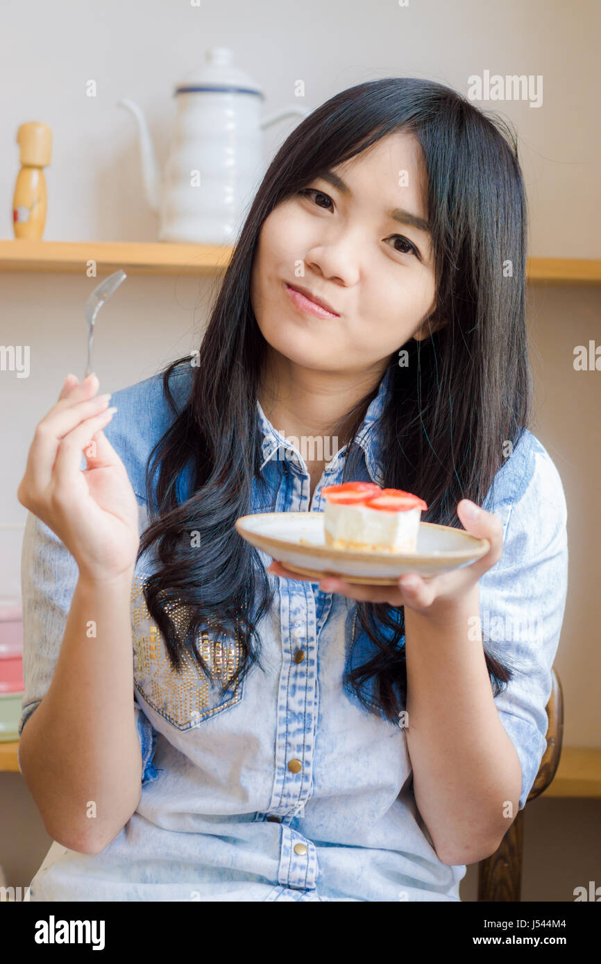 Beautiful smiling young woman biting strawberry cake in bakery shop ...