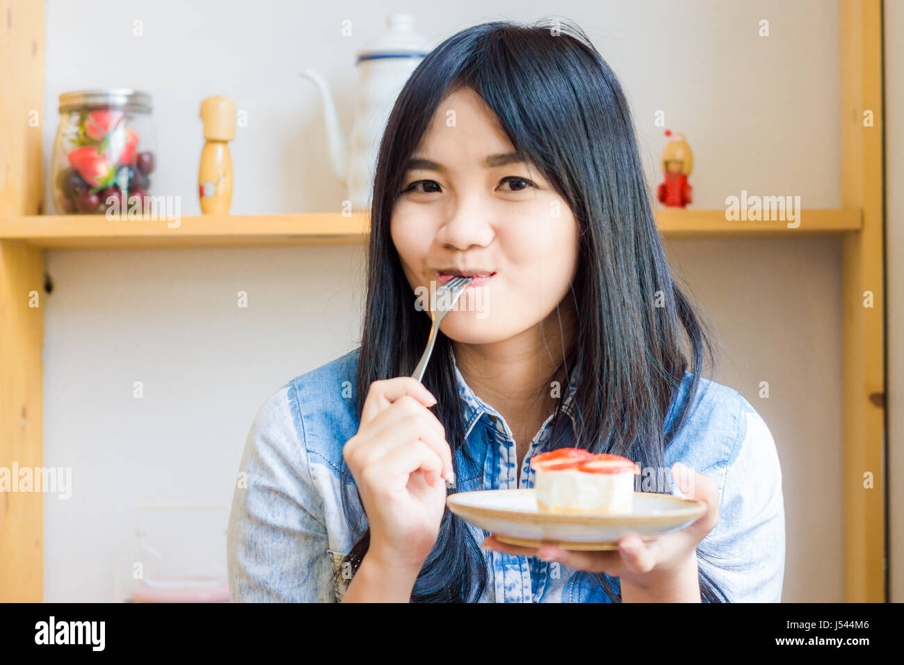 Asian smiling woman wearing jean shirt biting the piece of tasty ...