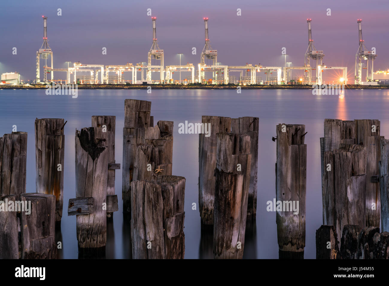 Old pylons from a pier, during sunset, with an industrial background at ...