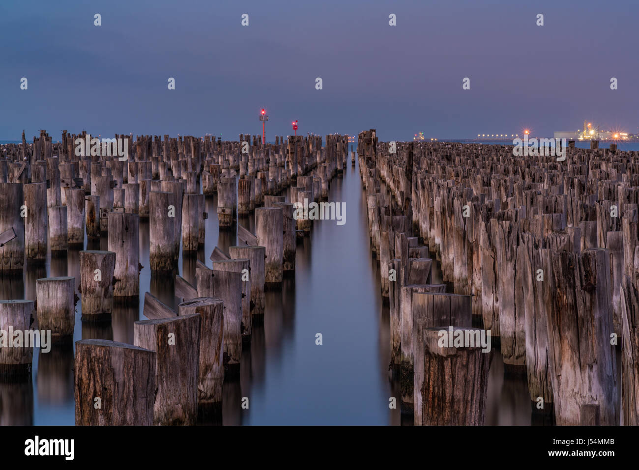 Old pylons from a pier, during sunset, with an industrial background at ...