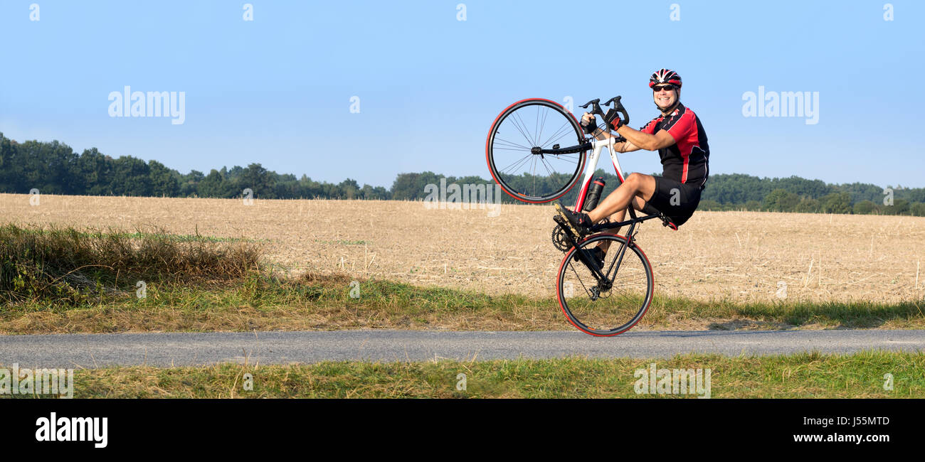 Cheerful cyclist riding on the rear wheel. Biker balancing while ...