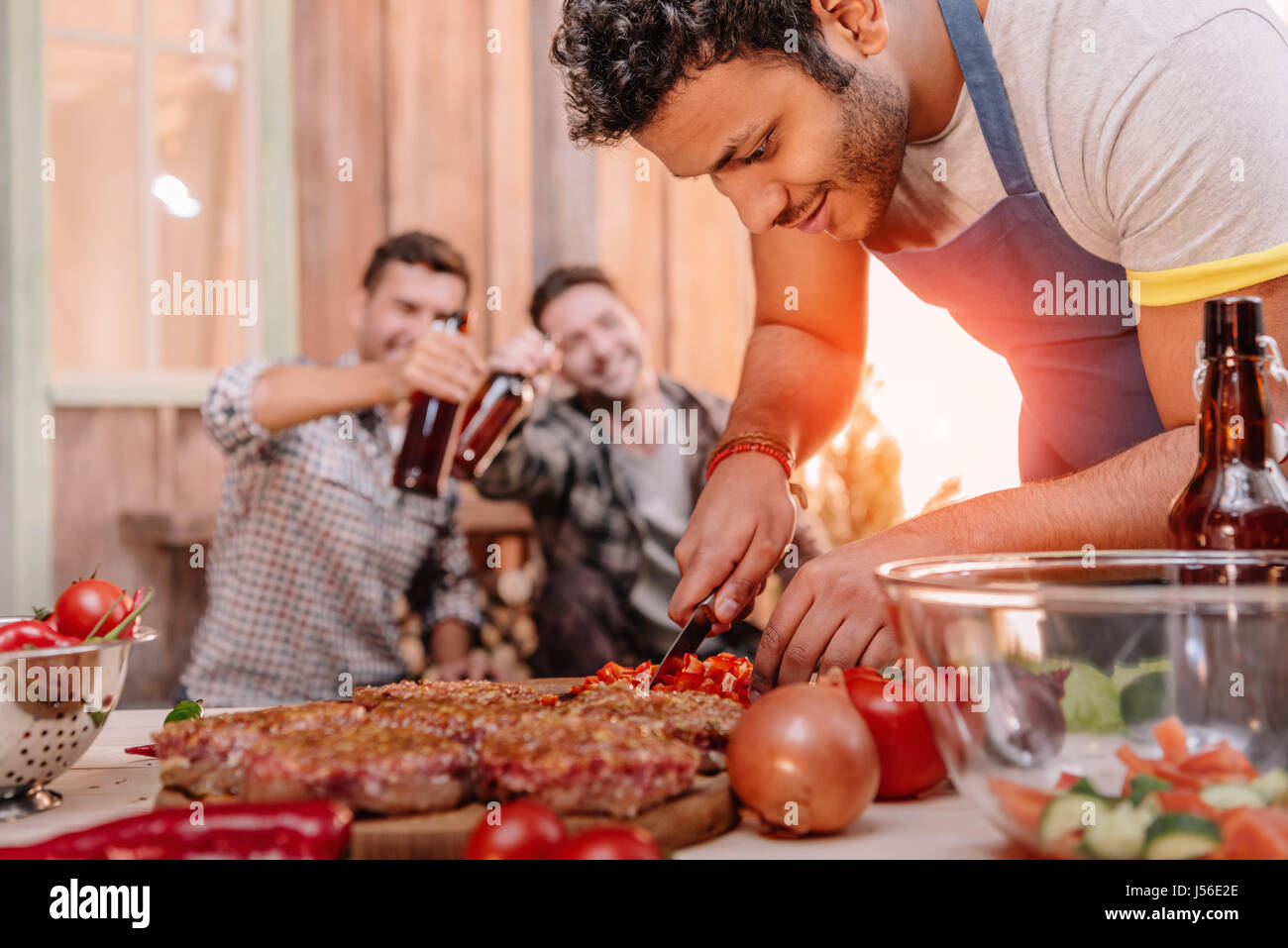man making burgers while his friends drinking beer sitting behind on ...