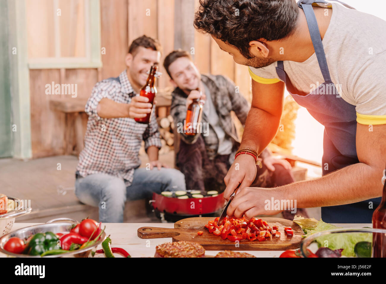 man making burgers while his friends drinking beer sitting behind on ...