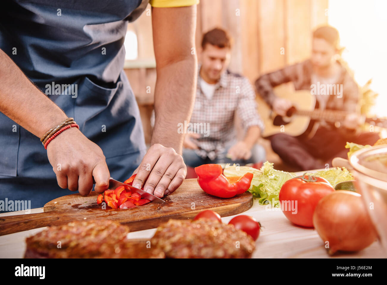 man making burgers while his friends with guitar sitting behind on ...